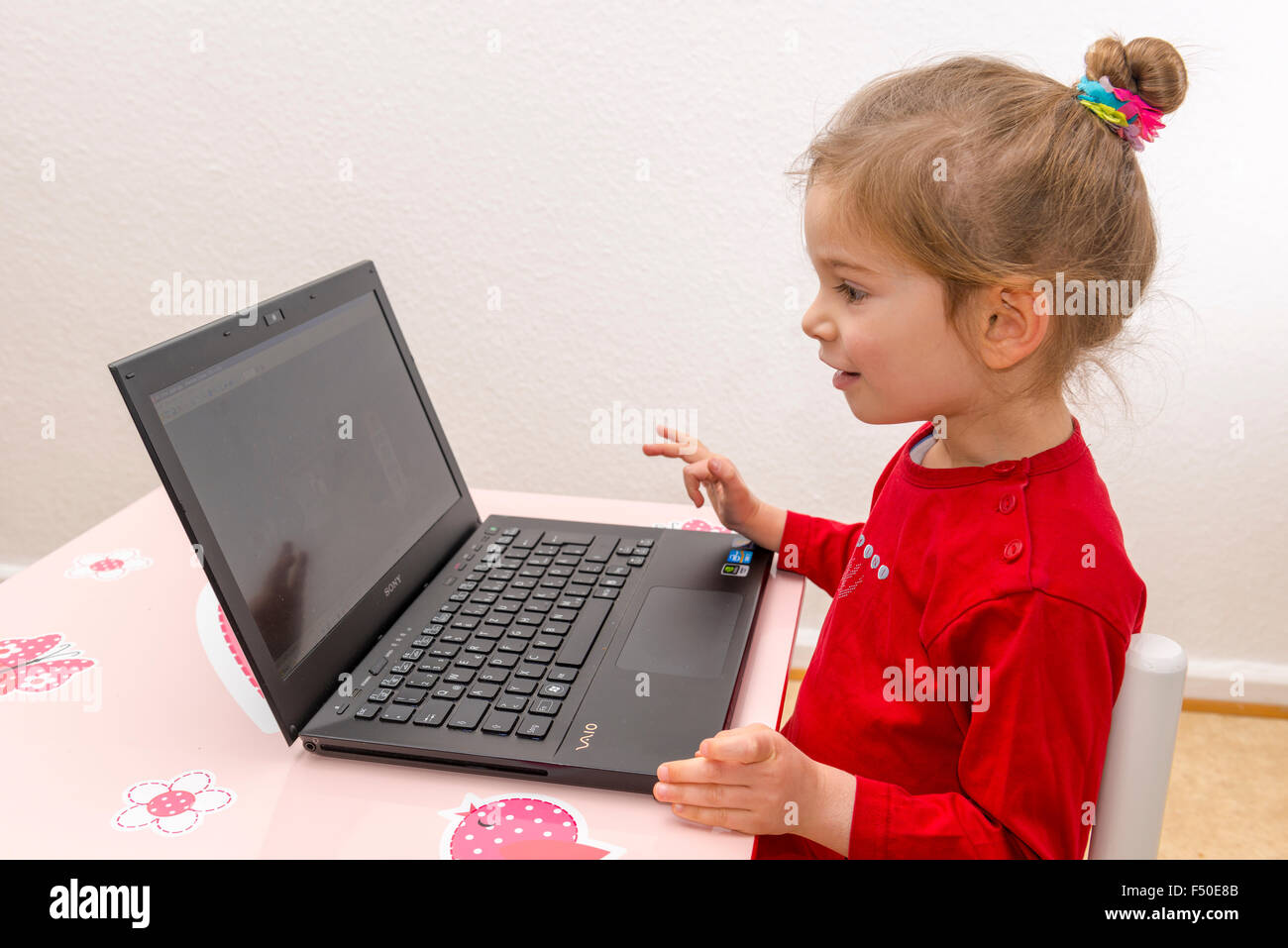 A blond three year old girl is sitting in front of a notebook, laptop ...