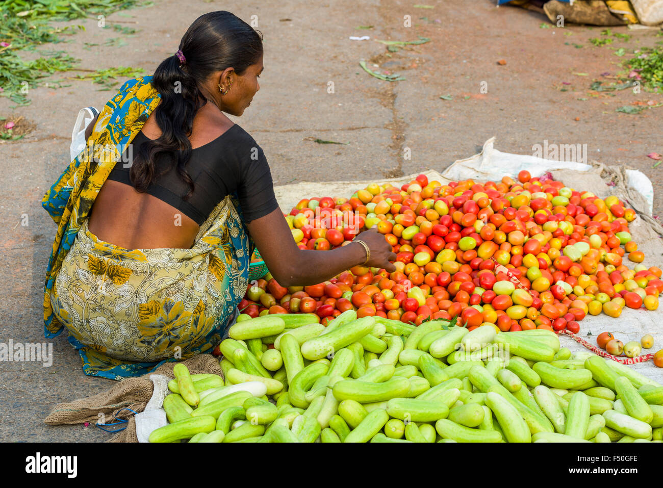 A woman is selling tomatoes and cucumbers at the weekly vegetable ...