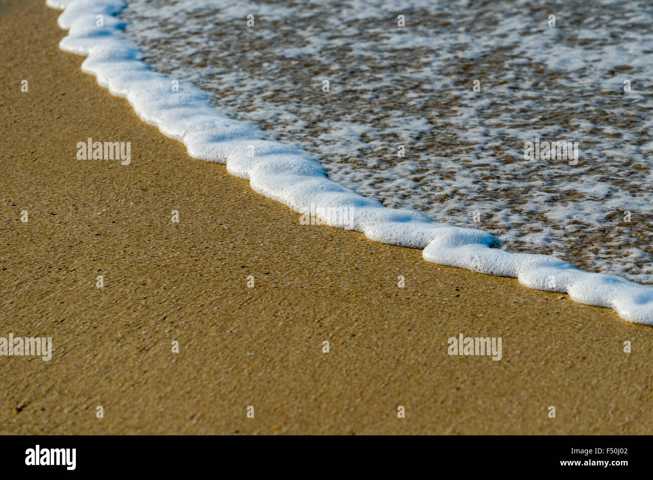 The froth of a breaking wave of blue sea water on the sand at Palolem ...