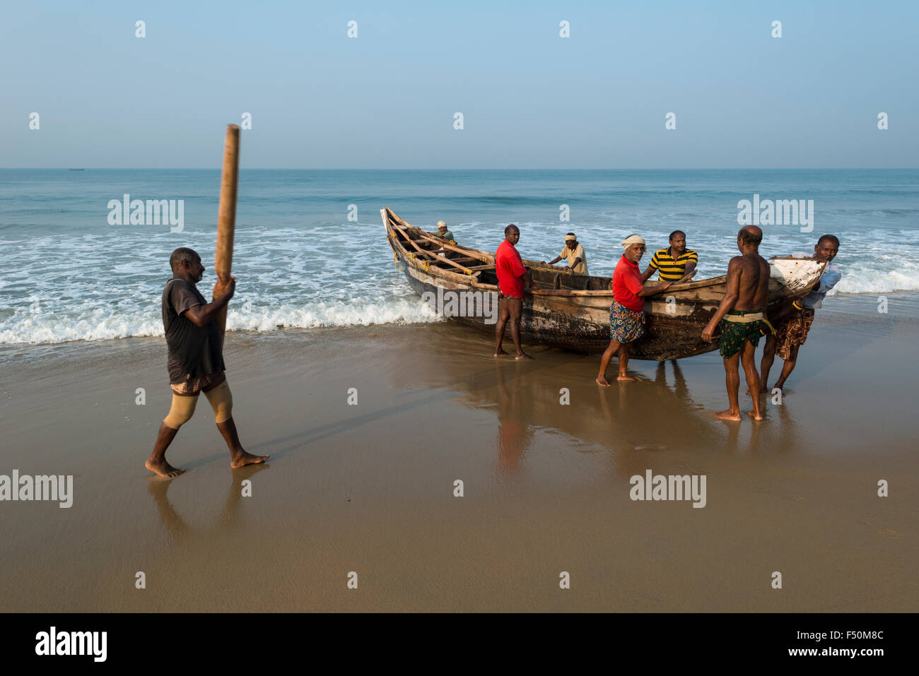 A group of fishermen is pulling a boat out of the sea onto the beach ...