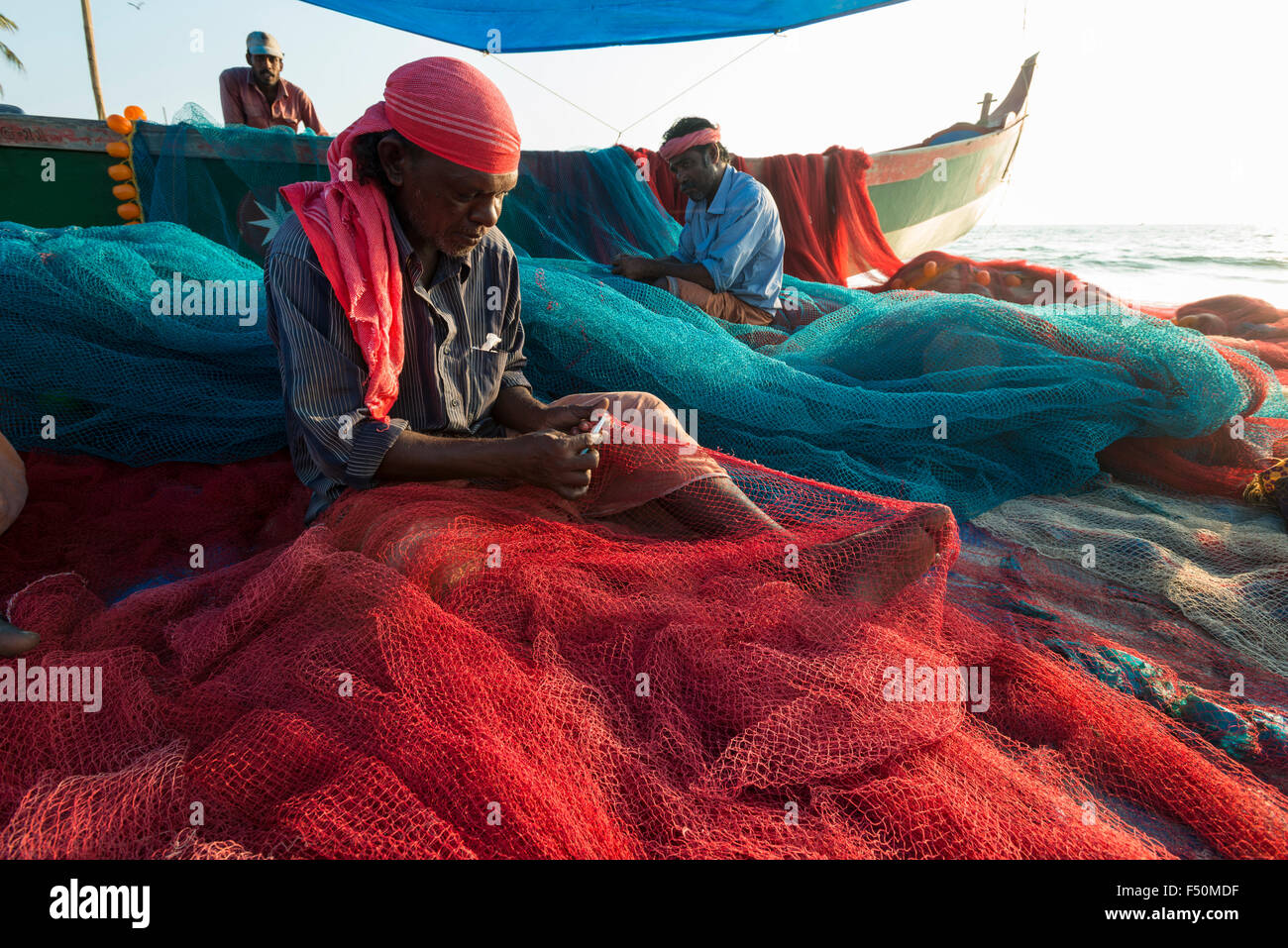 Two fishermen are repairing red and blue fishing nets on the beach ...