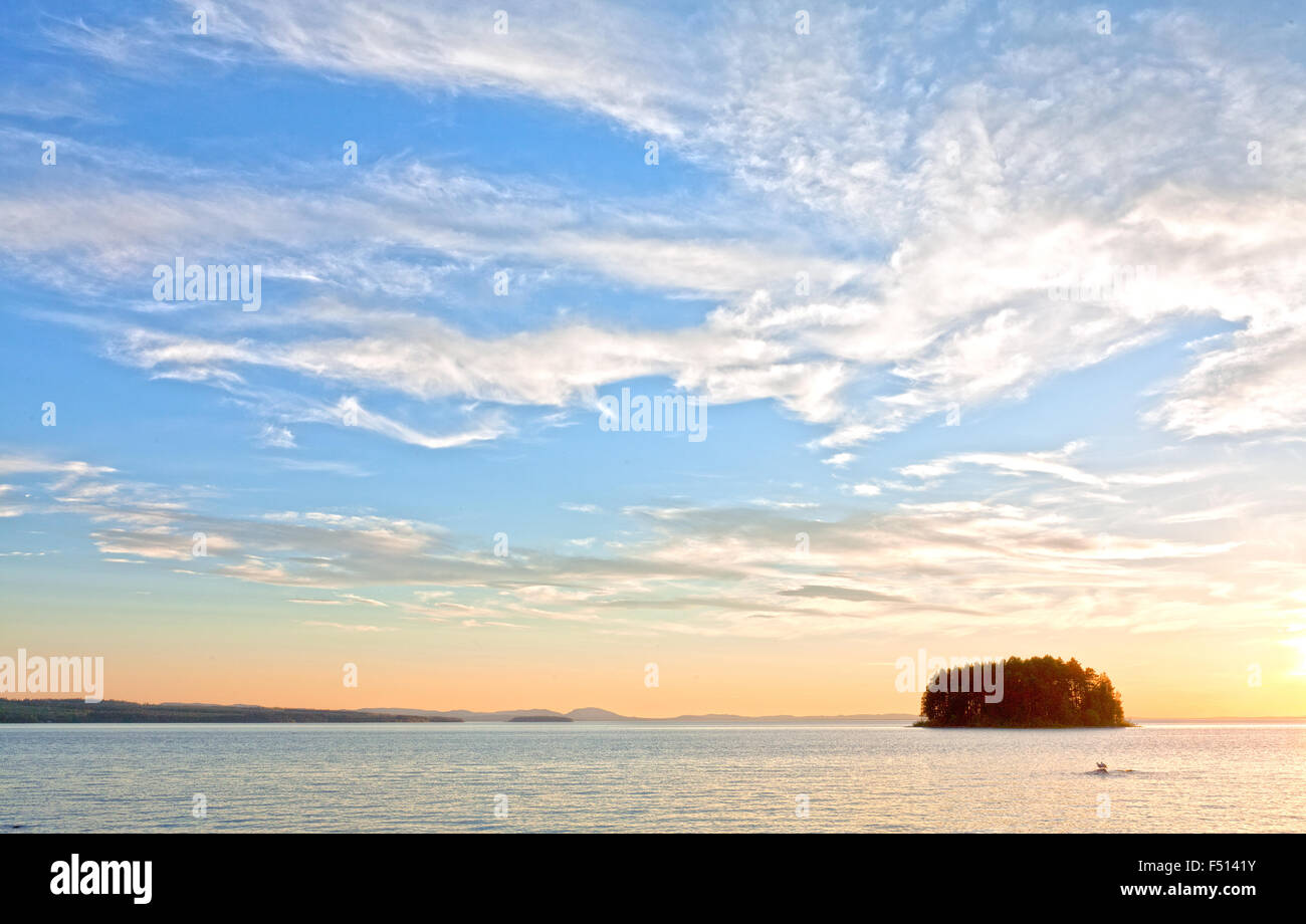 Island in a summer sunset. Wooded small island in a lake. Ridges at the ...