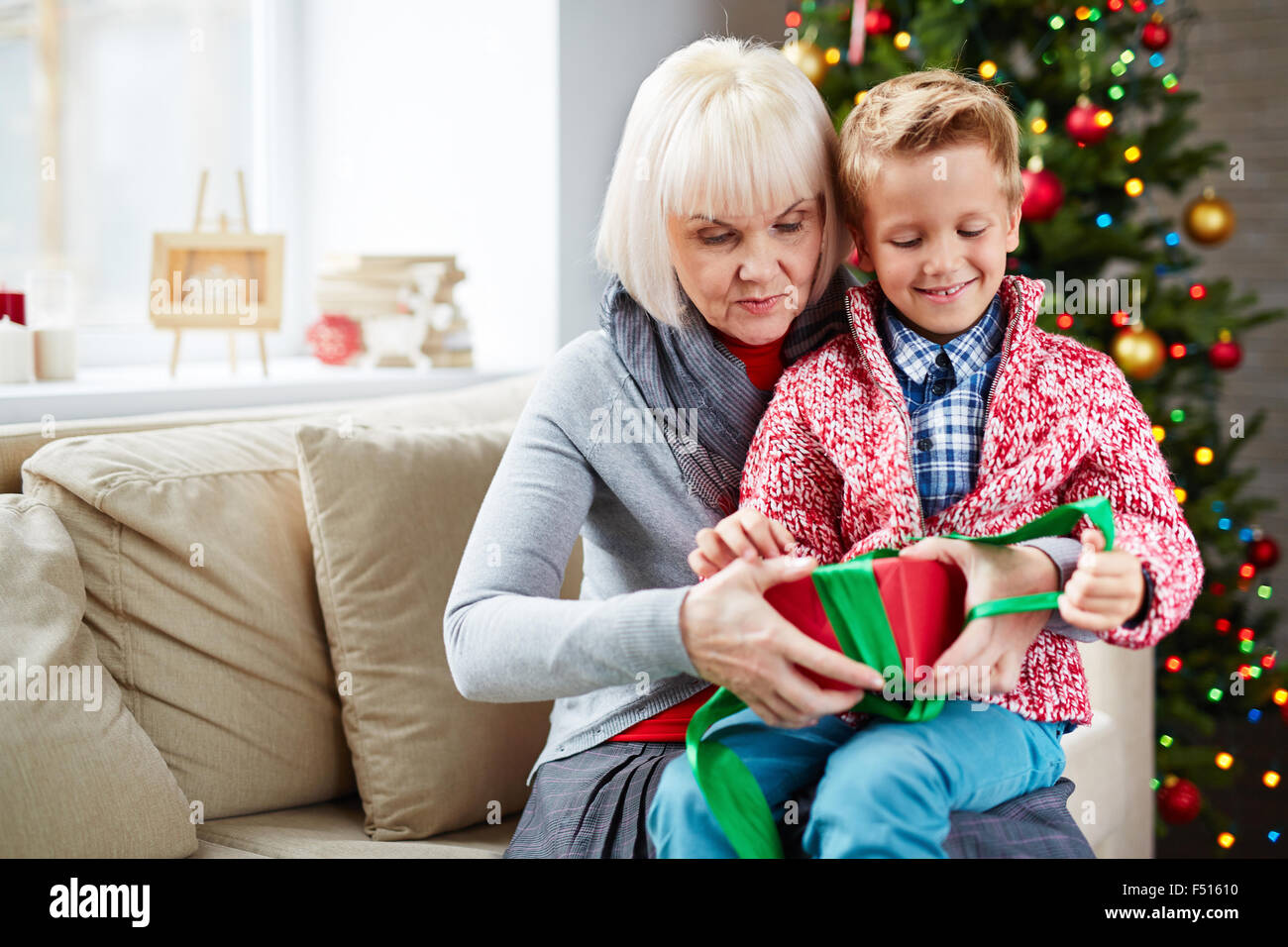 Mature woman helping her grandson untie gift-box on Christmas eve Stock ...