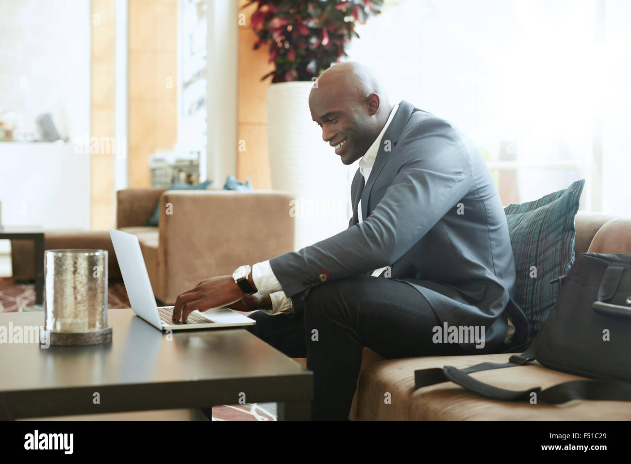 Happy businessman using laptop in hotel lobby. African business ...
