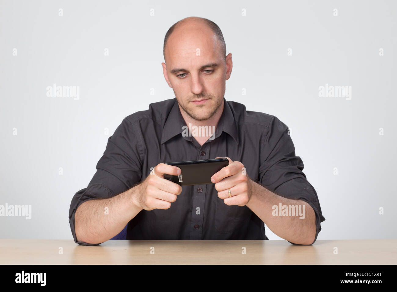 Man sat at desk playing on phone Stock Photo - Alamy