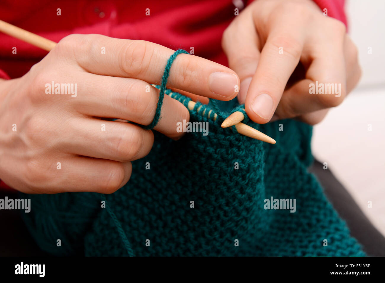 Closeup of woman's hands knitting with teal yarn on bamboo needles ...