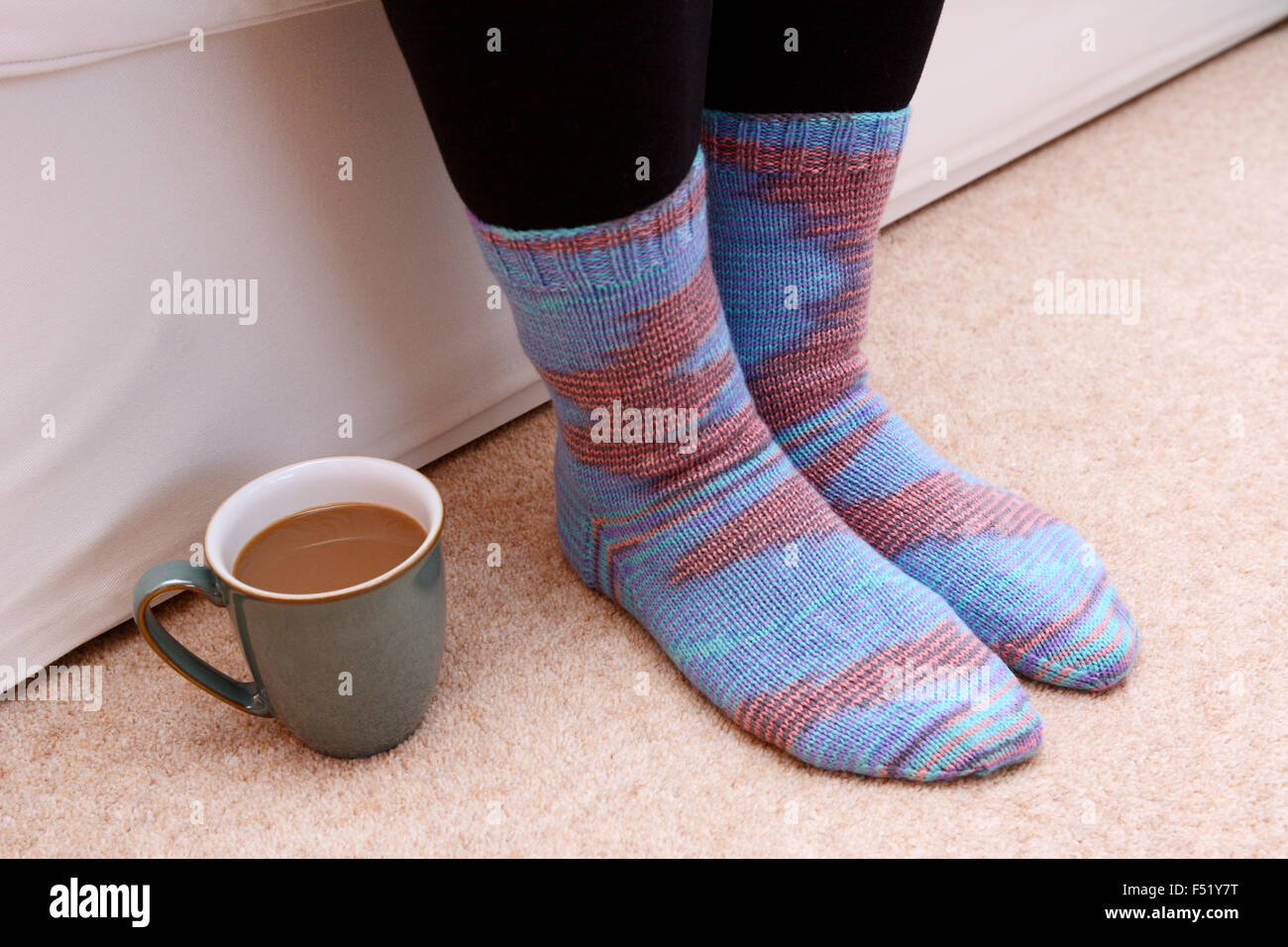 Cup of hot tea or coffee on the floor by a woman's feet in knitted ...