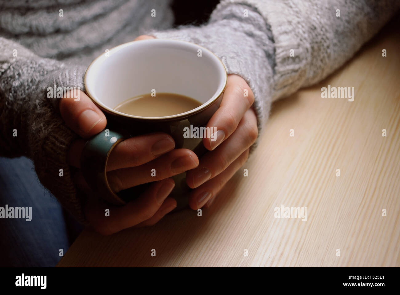 Woman holds hot cup of tea or coffee, warming her hands, sat at a ...