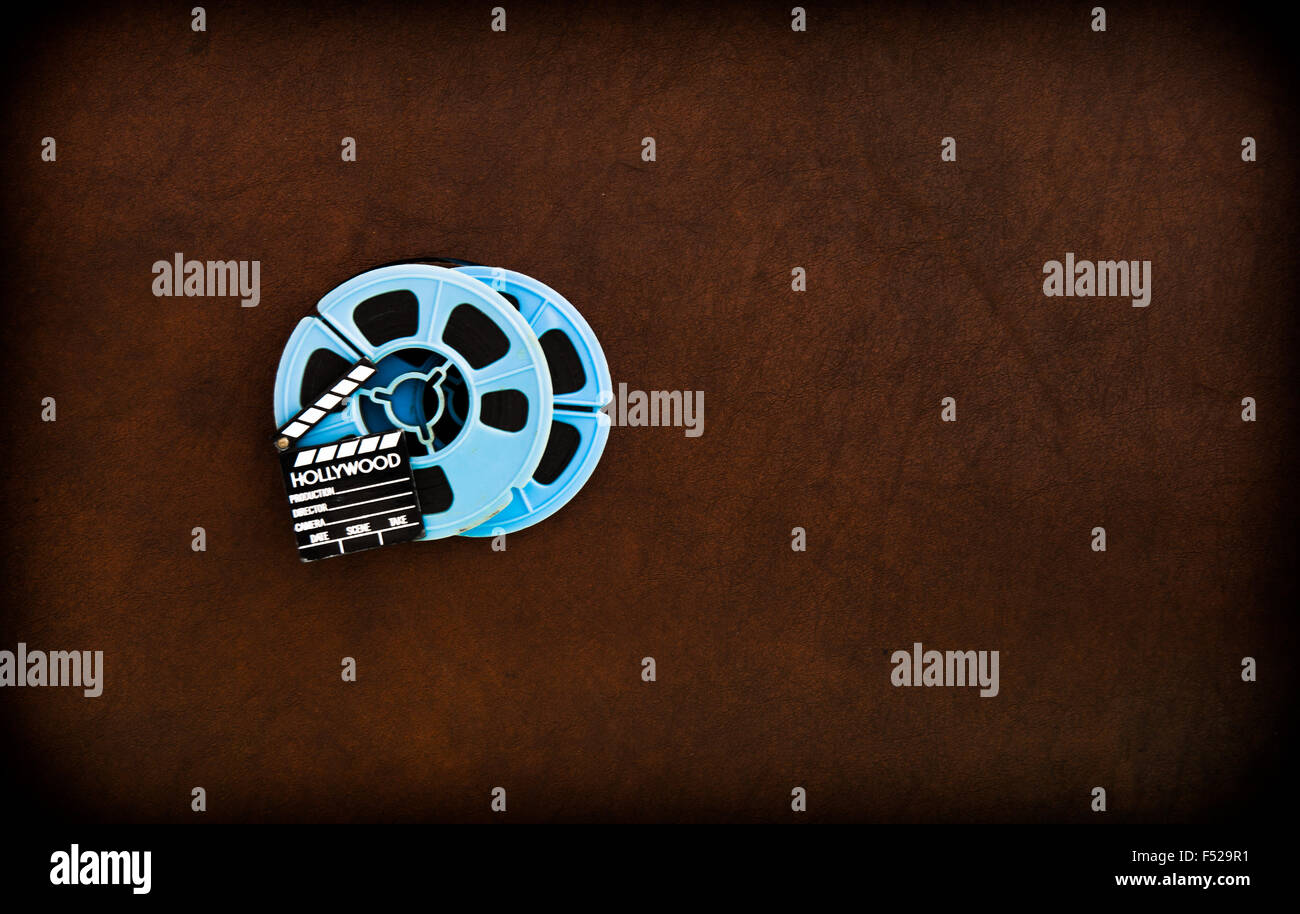 Little movie clapper board and blue colored film reels on brown table ...