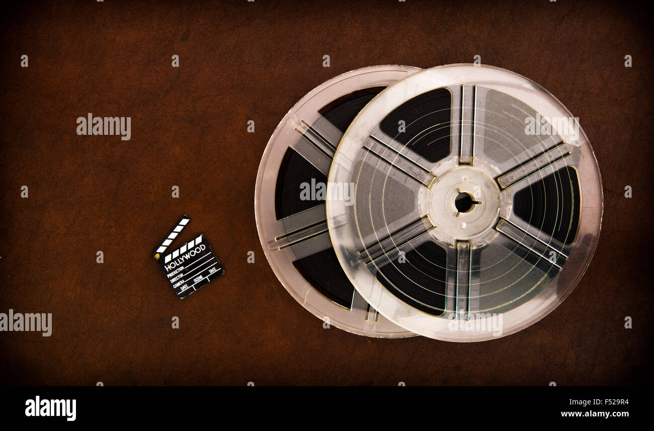 Little movie clapper board and transpared film reels on brown table ...