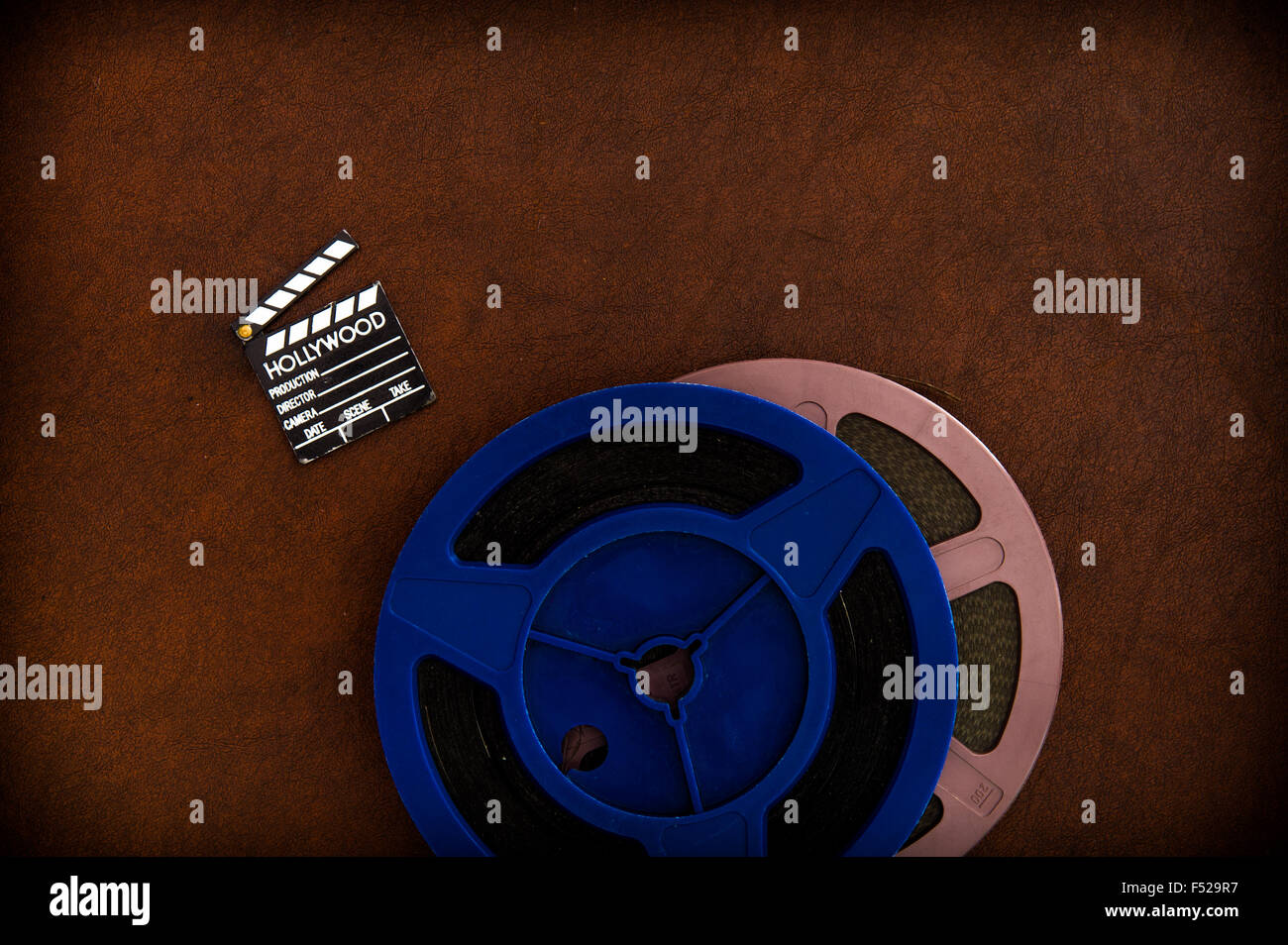 Little movie clapper board detail and colored film reels on brown table ...