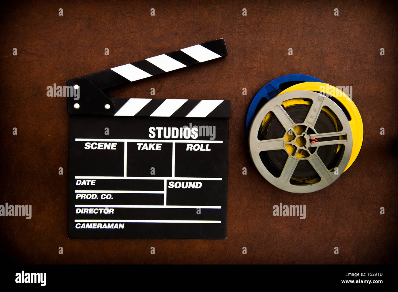 Movie clapper board and colored film reels on brown table Stock Photo ...