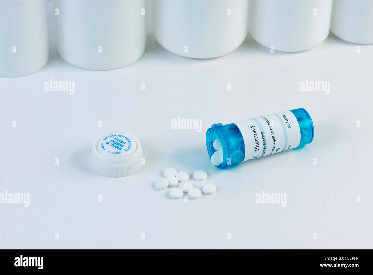 Blue prescription bottle with white pills and bottles in background ...