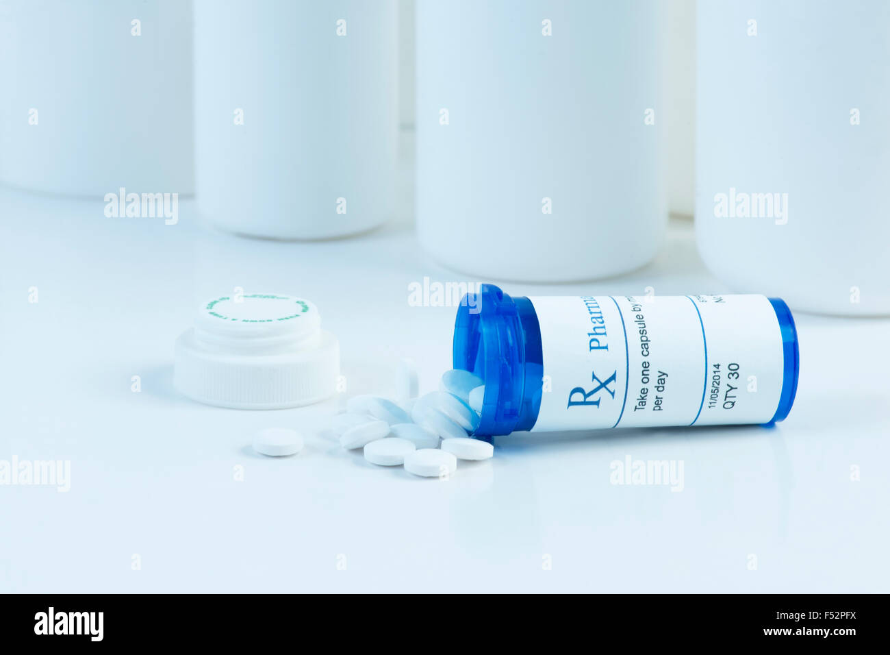 Blue prescription bottle with white pills and bottles in background ...