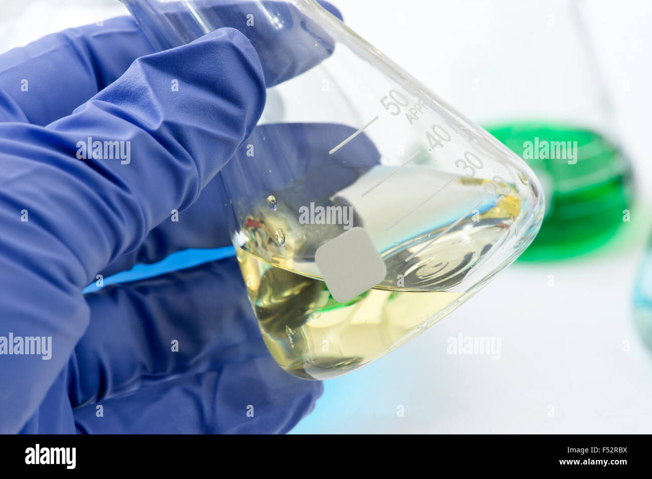 Technician with blue glove holds flask of light yellow reagent Stock ...