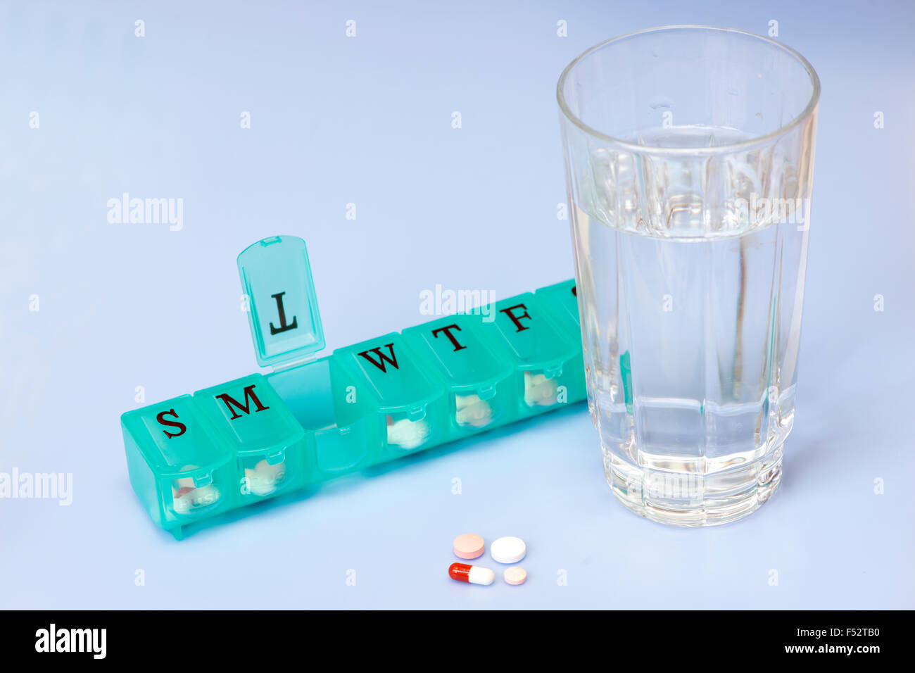 Daily pill dispenser with pills and glass of water Stock Photo - Alamy