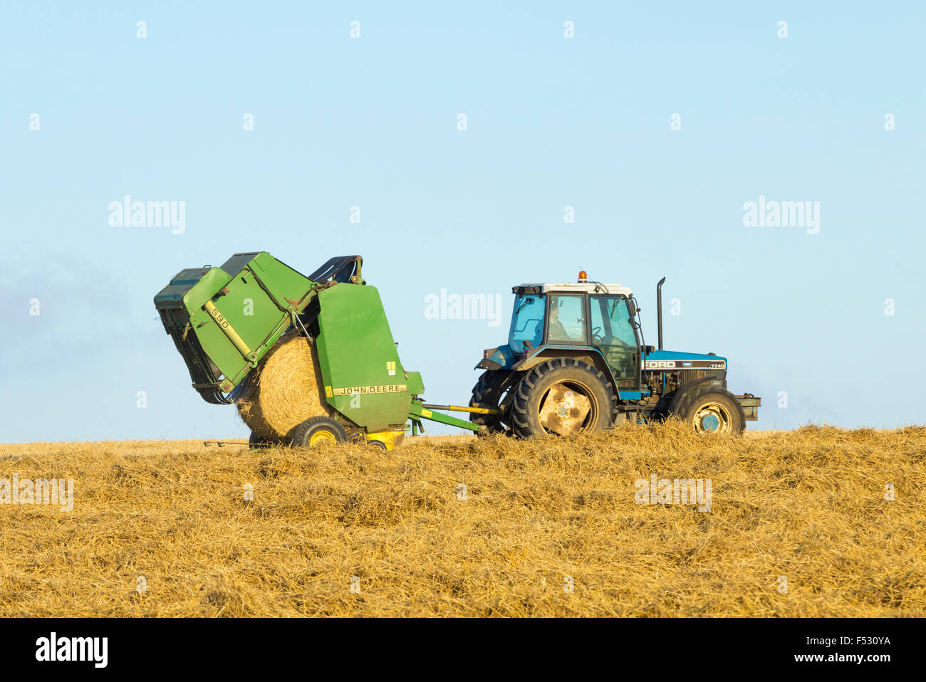 Farmer making round hay bales with John Deere baler. England, UK Stock ...