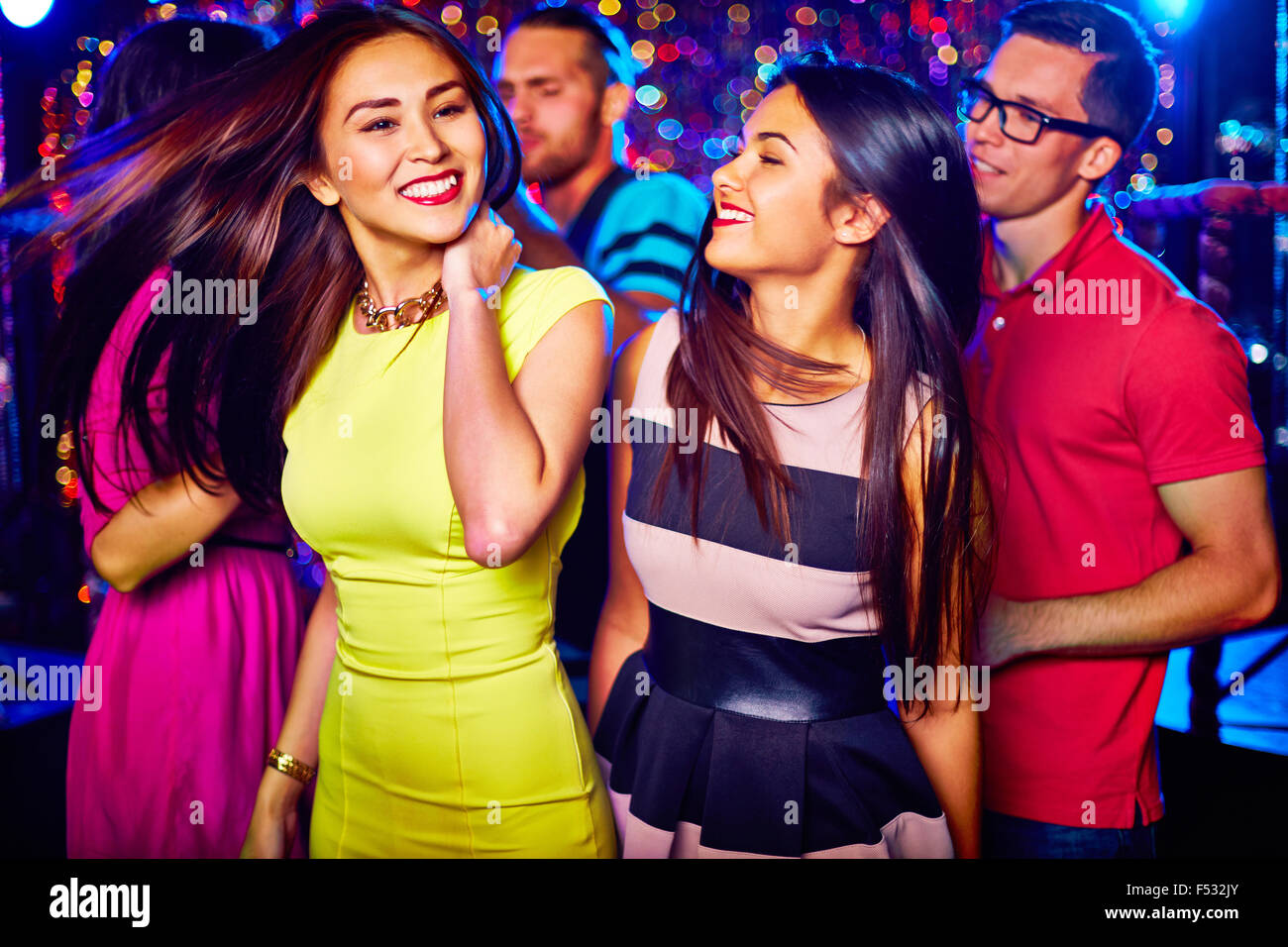 Two happy girls dancing in nightclub on background of their friends ...