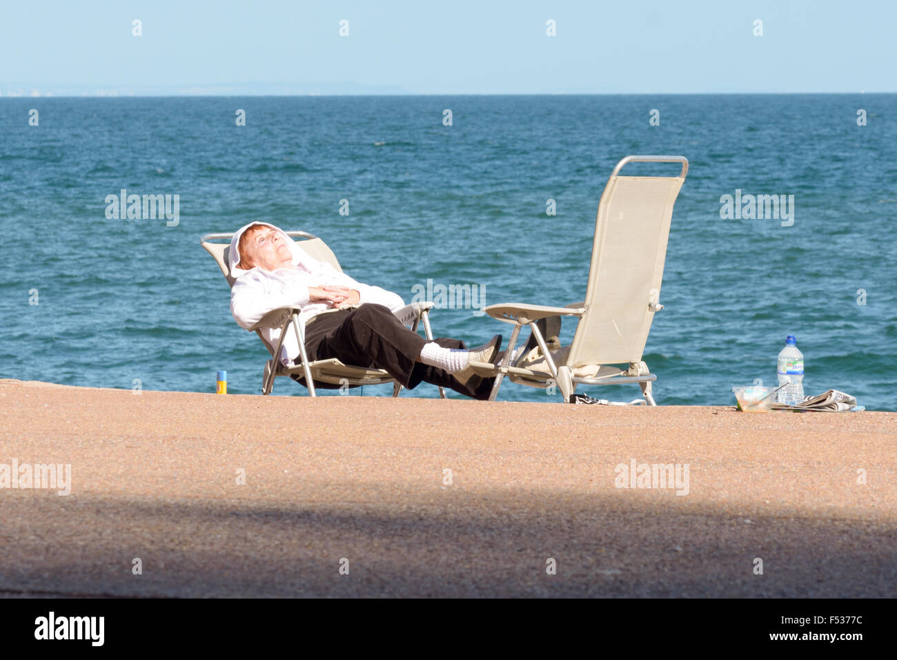 Elderly lady reclined on deck-chair sunbathing on hot September day at ...