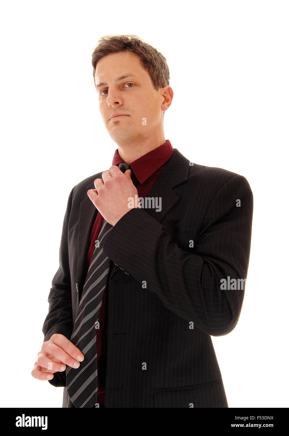 A business man standing in a suit and fixing his tie, looking serious ...