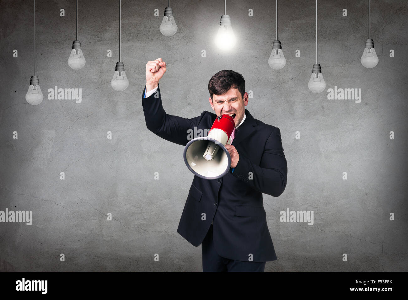 Businessman with megaphone stands in a gray room with hanging bulbs ...