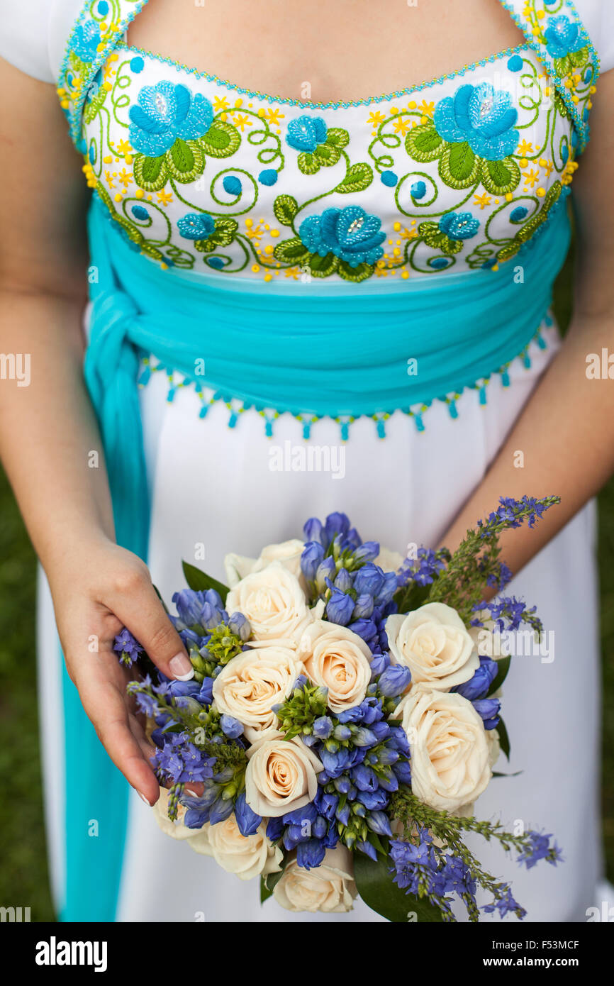 bride in blue dress with embroidery holds a bouquet of white roses ...