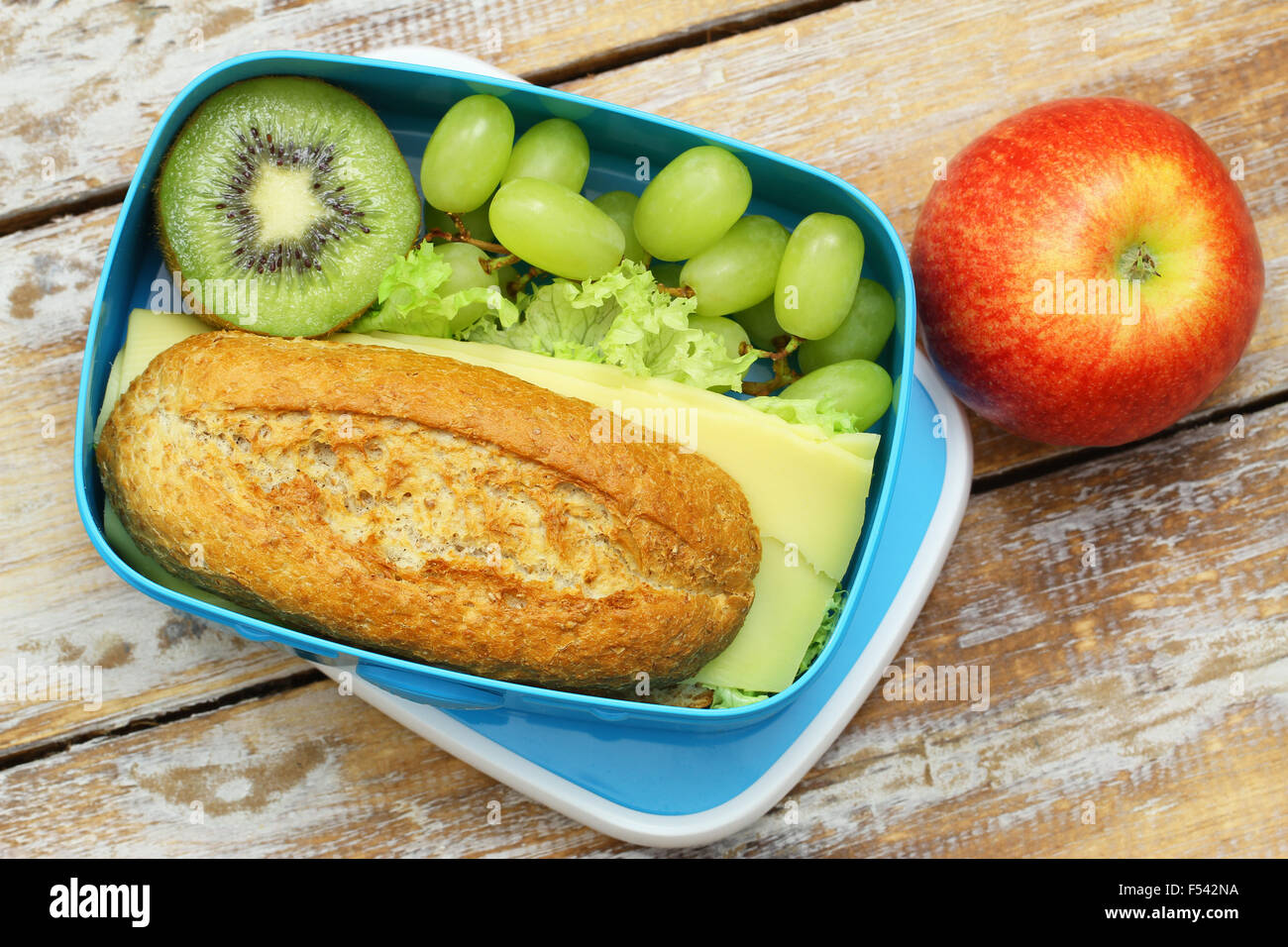 Packed lunch box containing brown cheese roll, grapes, kiwi fruit and ...