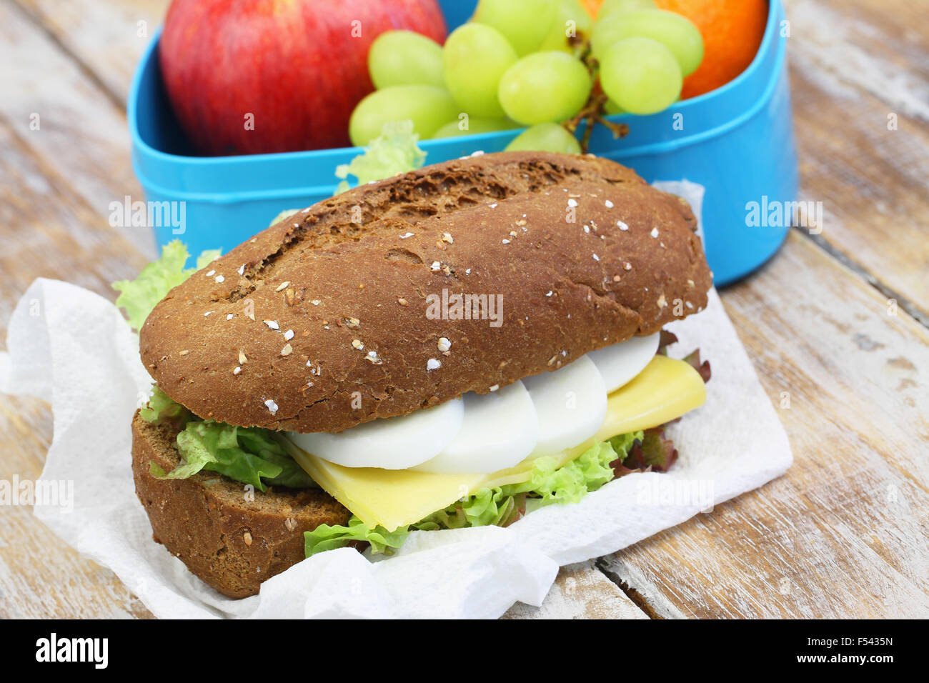 Brown bread roll with cheese, hard boiled egg, lettuce and lunch box ...