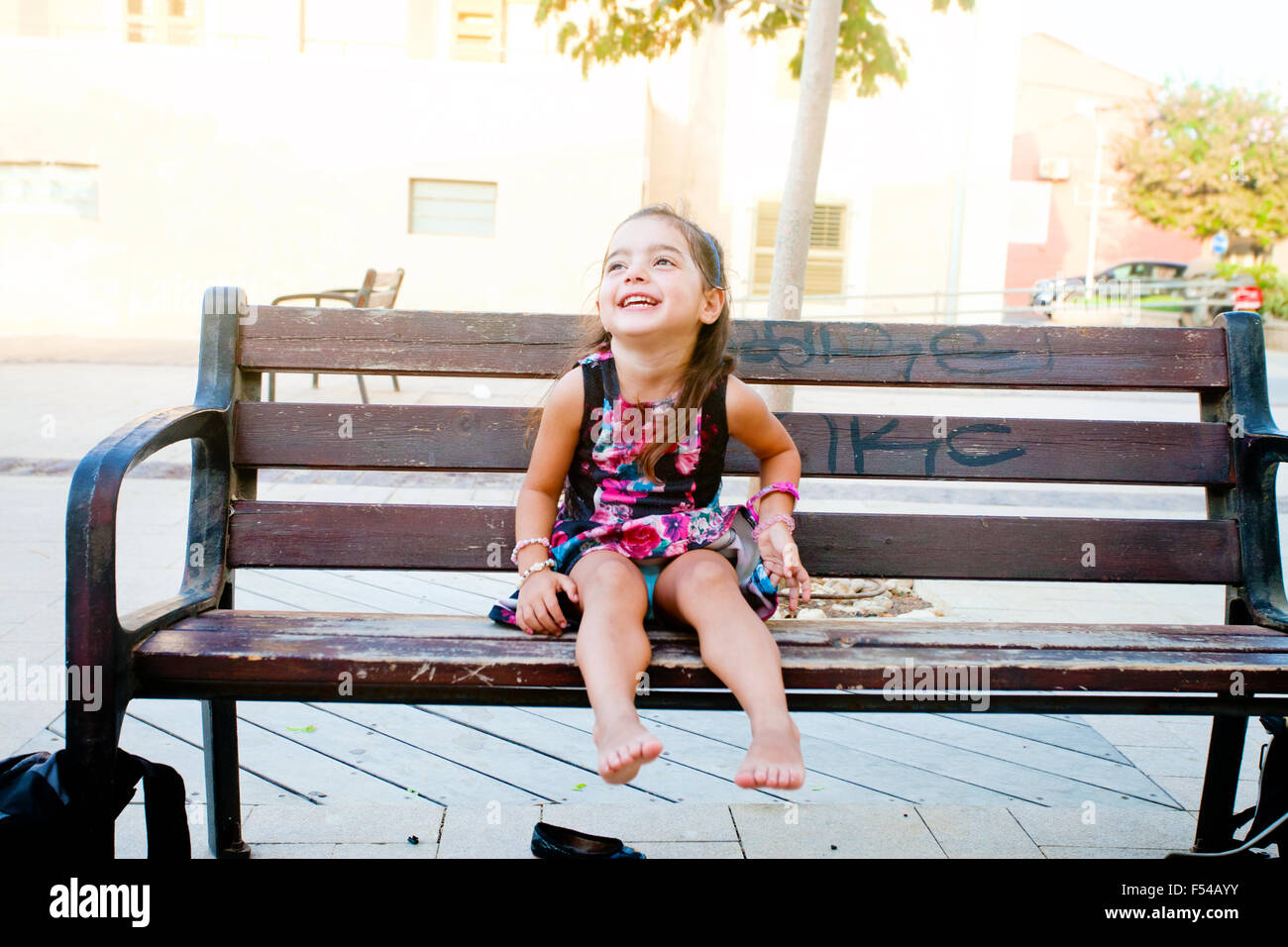Happy cute little girl sitting on a bench (sunset lighting Stock Photo ...