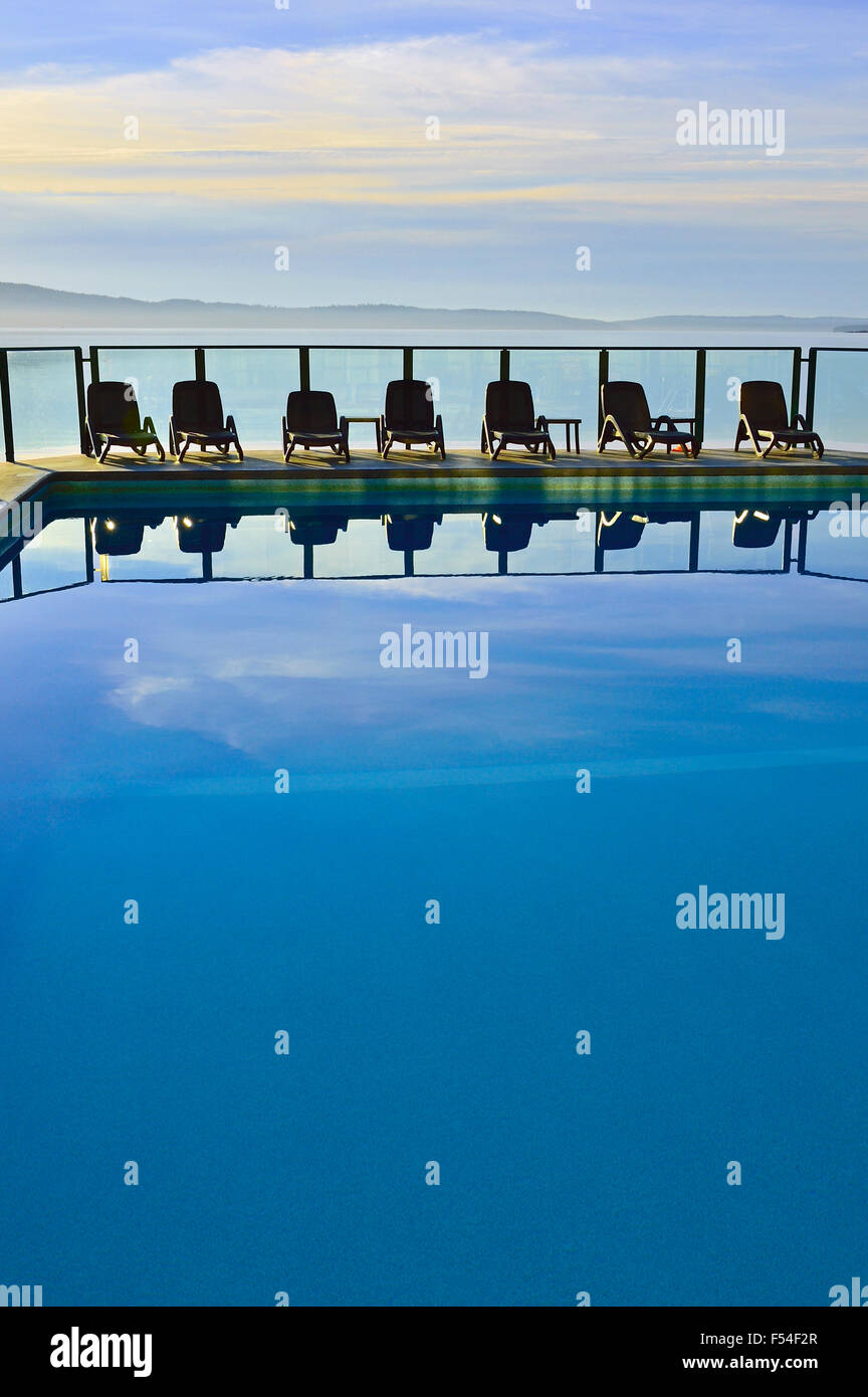 A vertical image of an outdoor swimming pool with a line of chairs ...
