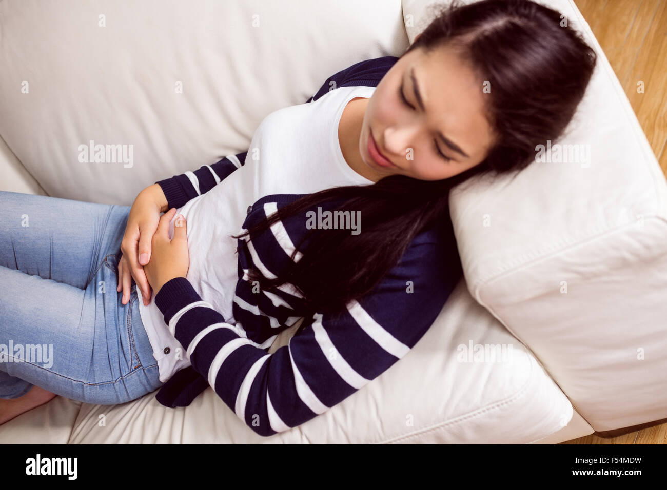 Asian woman lying on the couch with cramps Stock Photo - Alamy