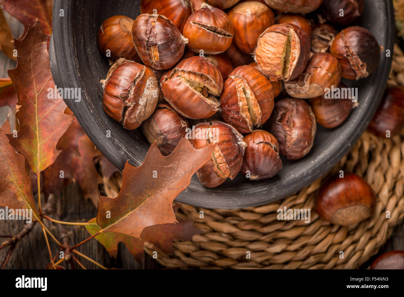 Roasted chestnuts on a rustic wooden table with autumn leaves in the ...