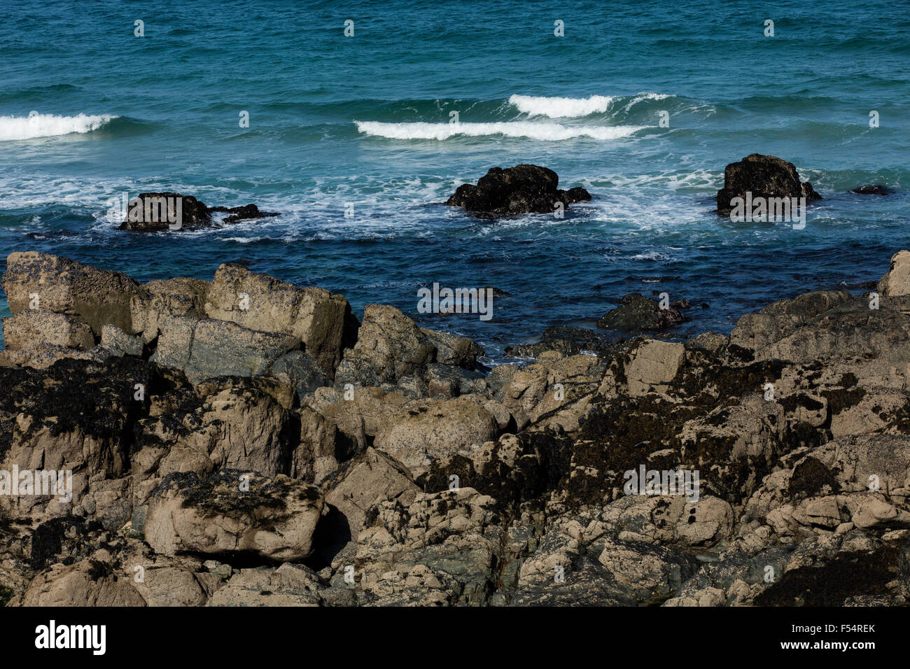 White water waves in bright blue sea break against the rocks off the ...