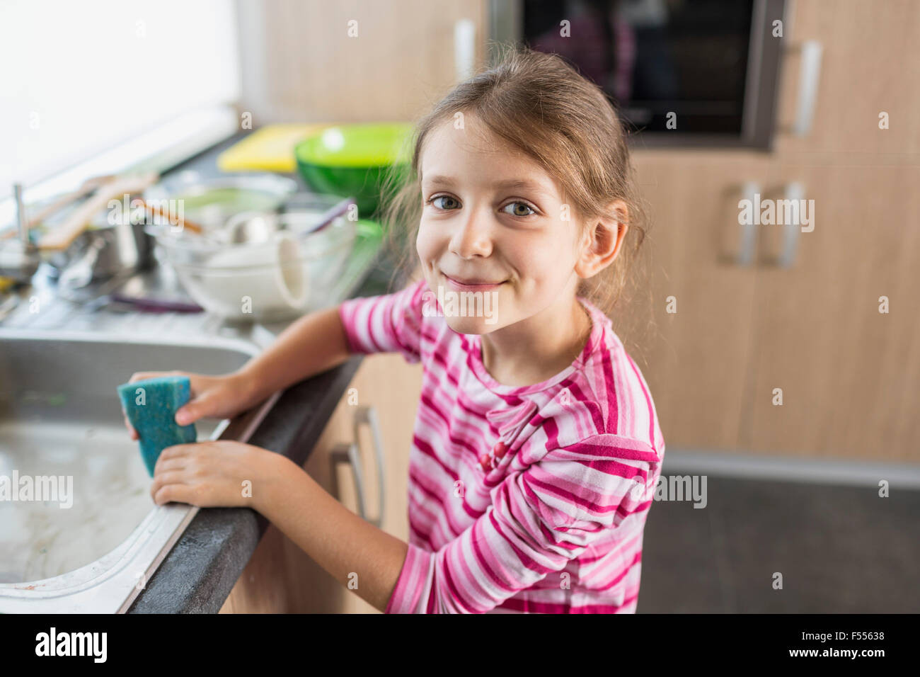 Portrait of smiling girl holding cleaning sponge at kitchen sink Stock ...