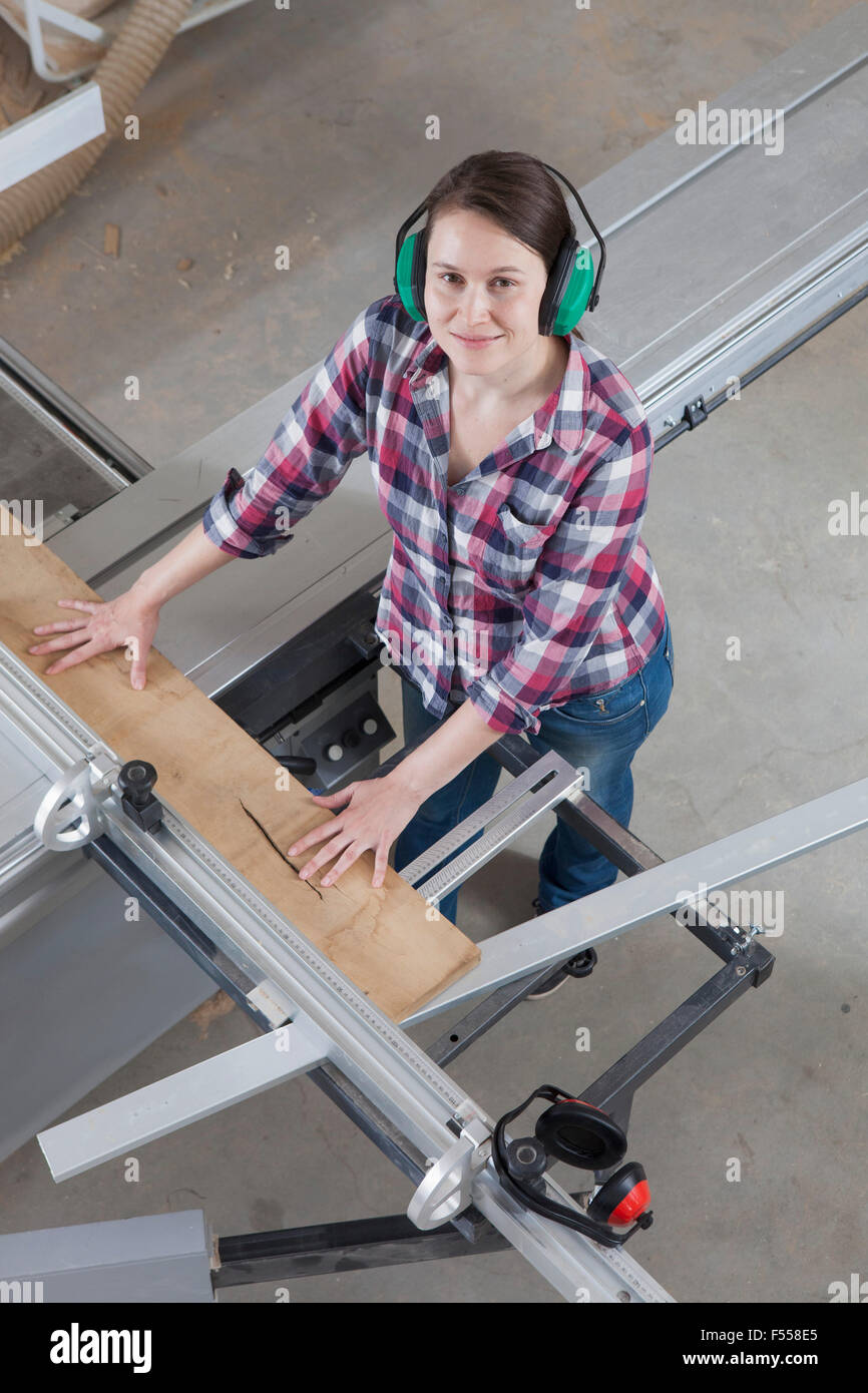 High angle portrait of happy female carpenter using a sliding table saw ...