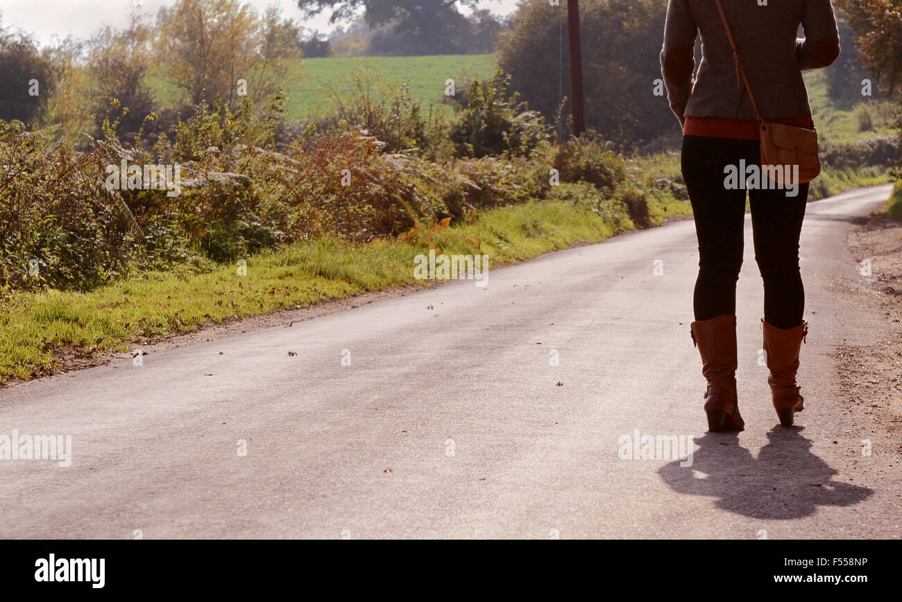 Fashionably dressed young woman walks up a country lane alone in autumn ...