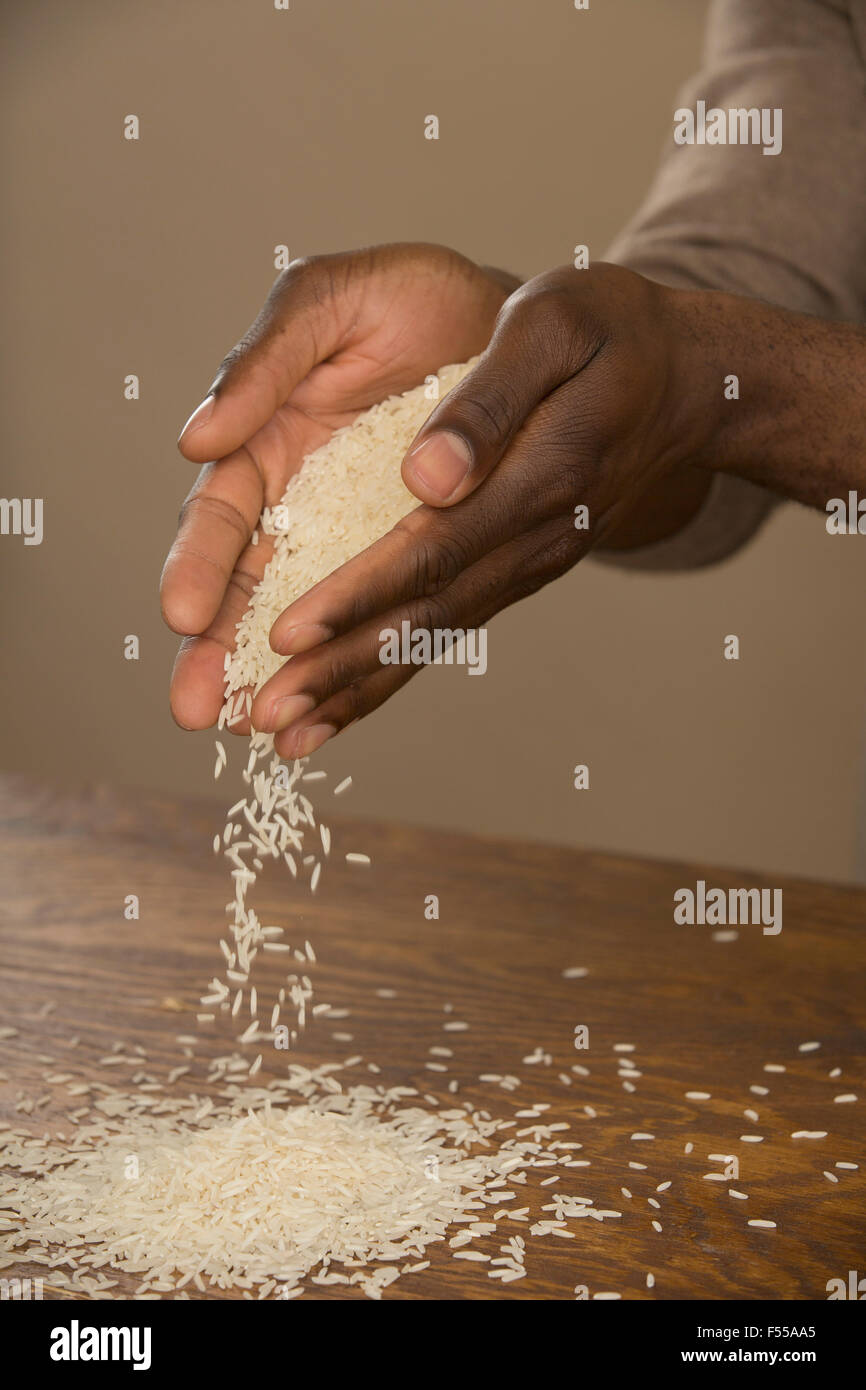 Hands pouring rice on table against colored background Stock Photo - Alamy