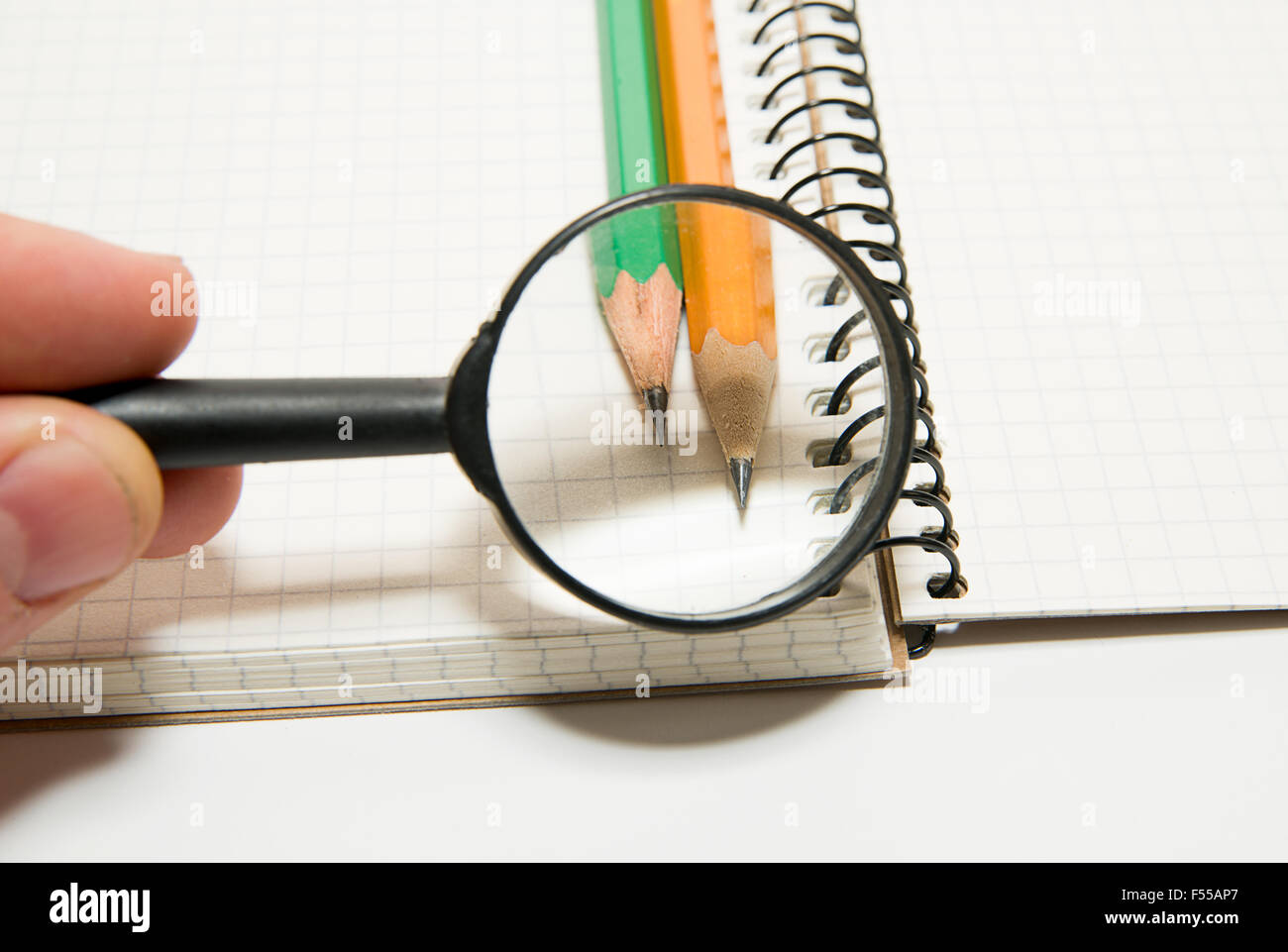 The hand with a magnifying glass and two pencils on over white Stock ...