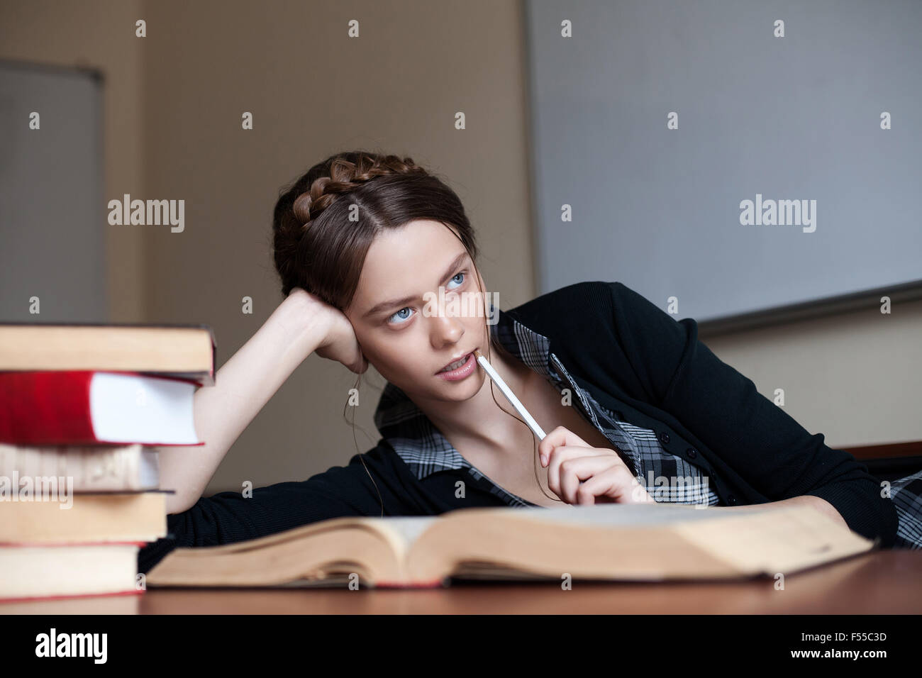Beautiful female student sitting at the table with books and thinking ...
