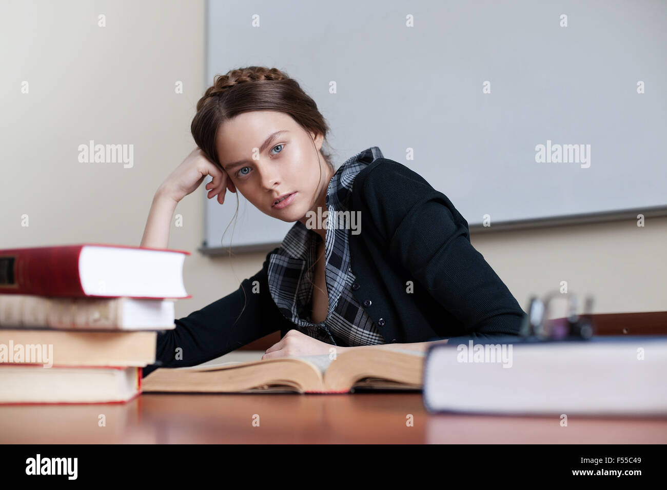 Beautiful female student sitting at the table with books and thinking ...