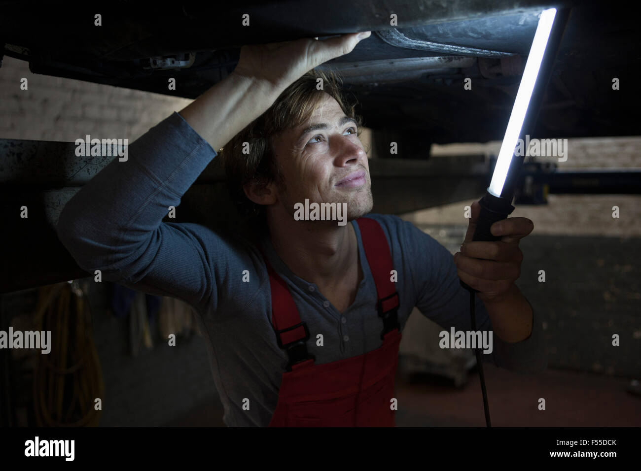 Mechanic holding illuminated fluorescent light while examining car ...