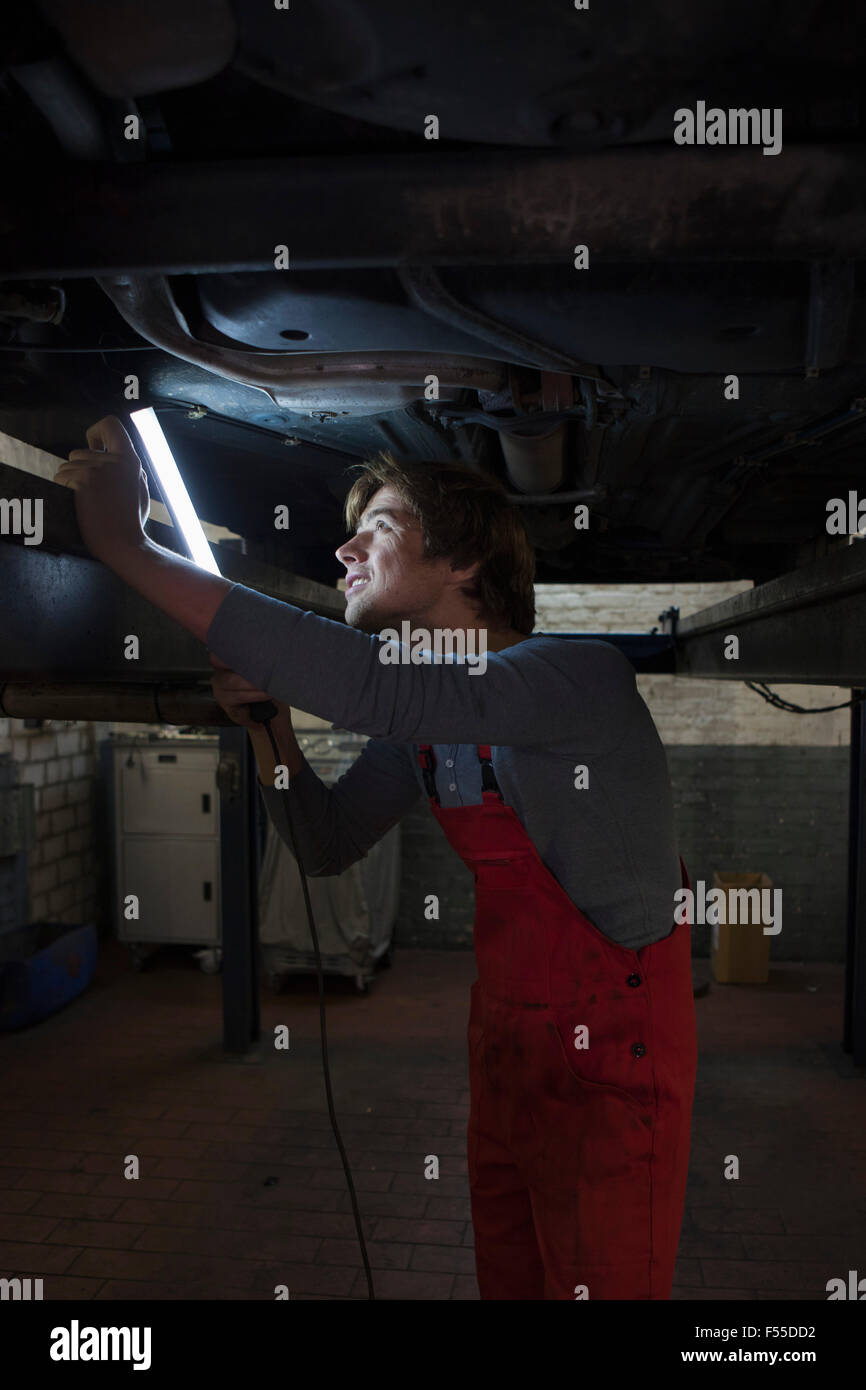 Mechanic holding illuminated fluorescent light while examining ...