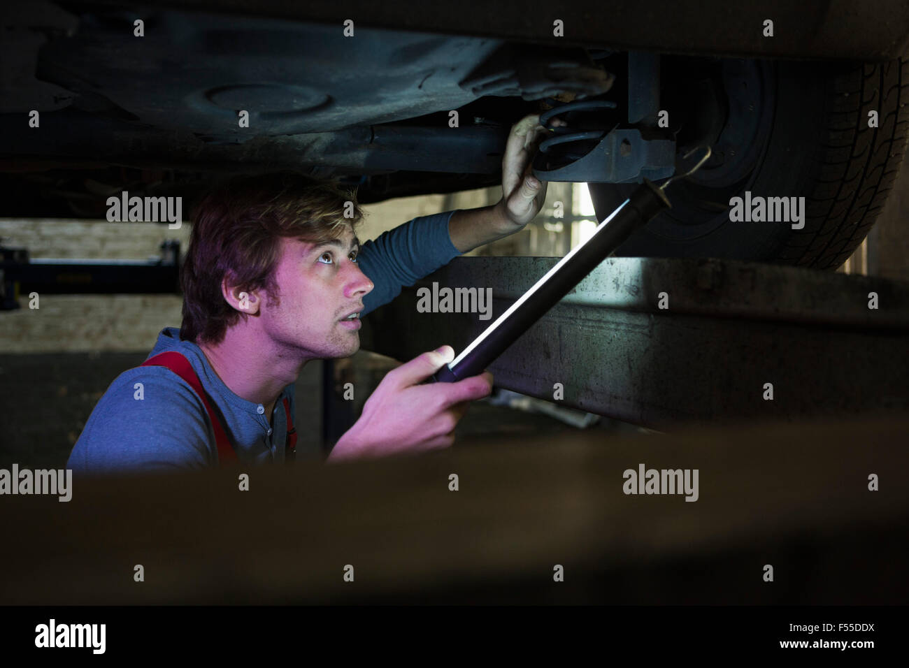 Mechanic with illuminated fluorescent light examining car from below ...