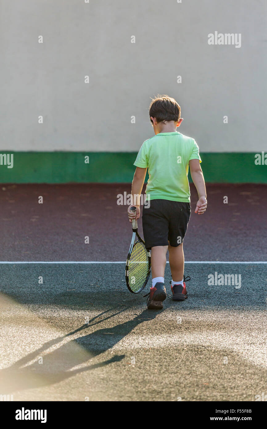 Rear view of boy holding tennis racket and walking at court Stock Photo ...