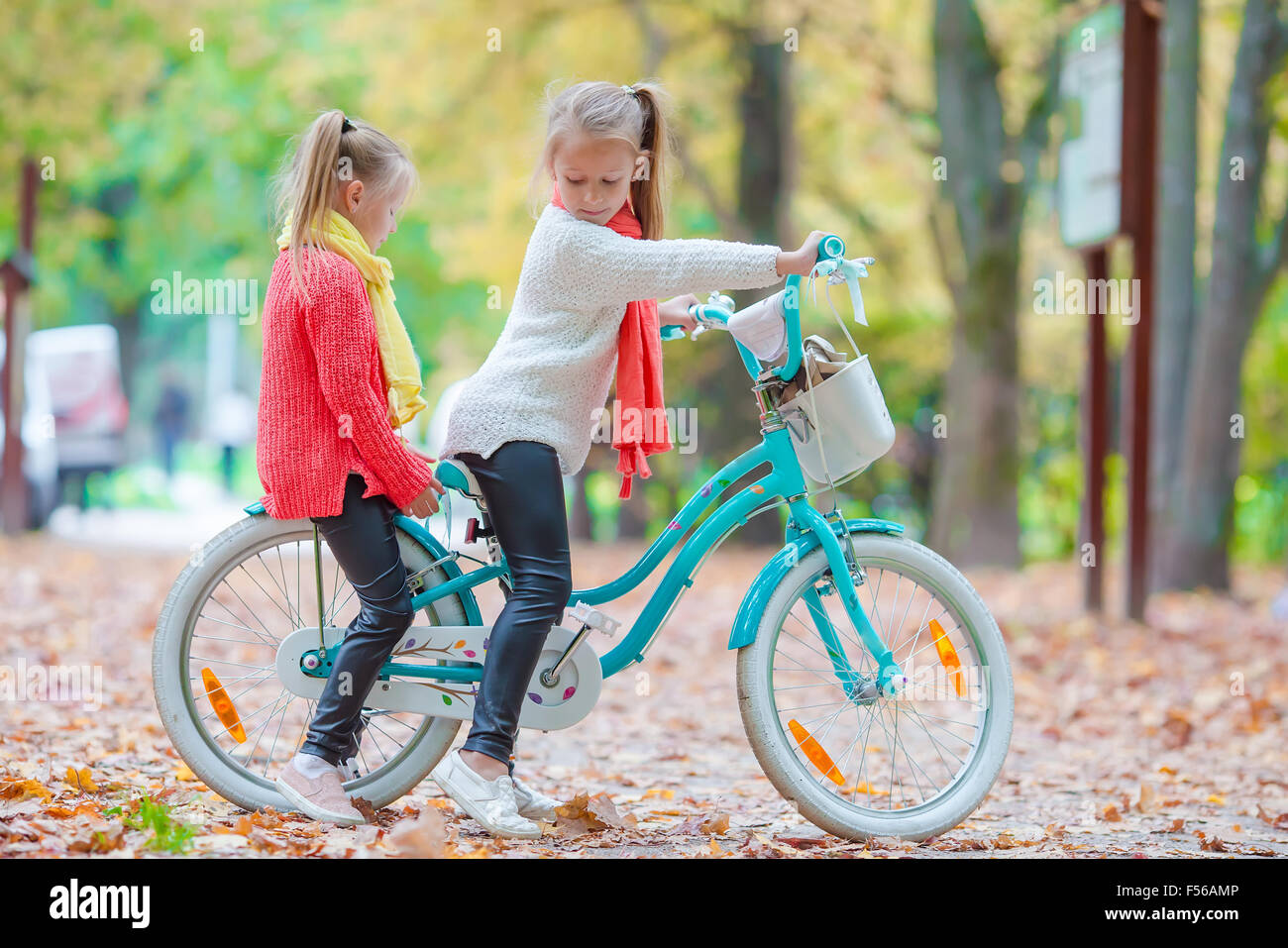 Adorable little girls riding a bike at beautiful autumn day outdoors ...