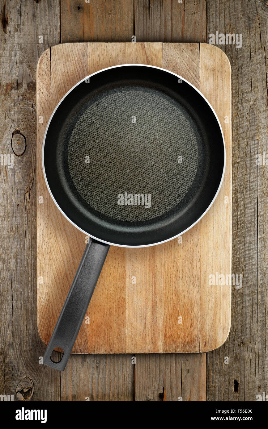 Frying pan on wooden chopping board top view Stock Photo - Alamy