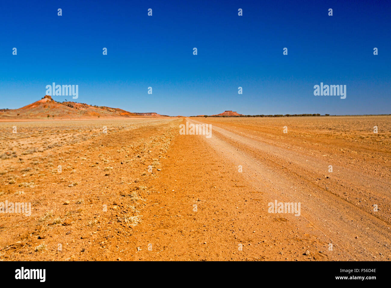 Long outback dirt road across treeless red plains with low hill on ...