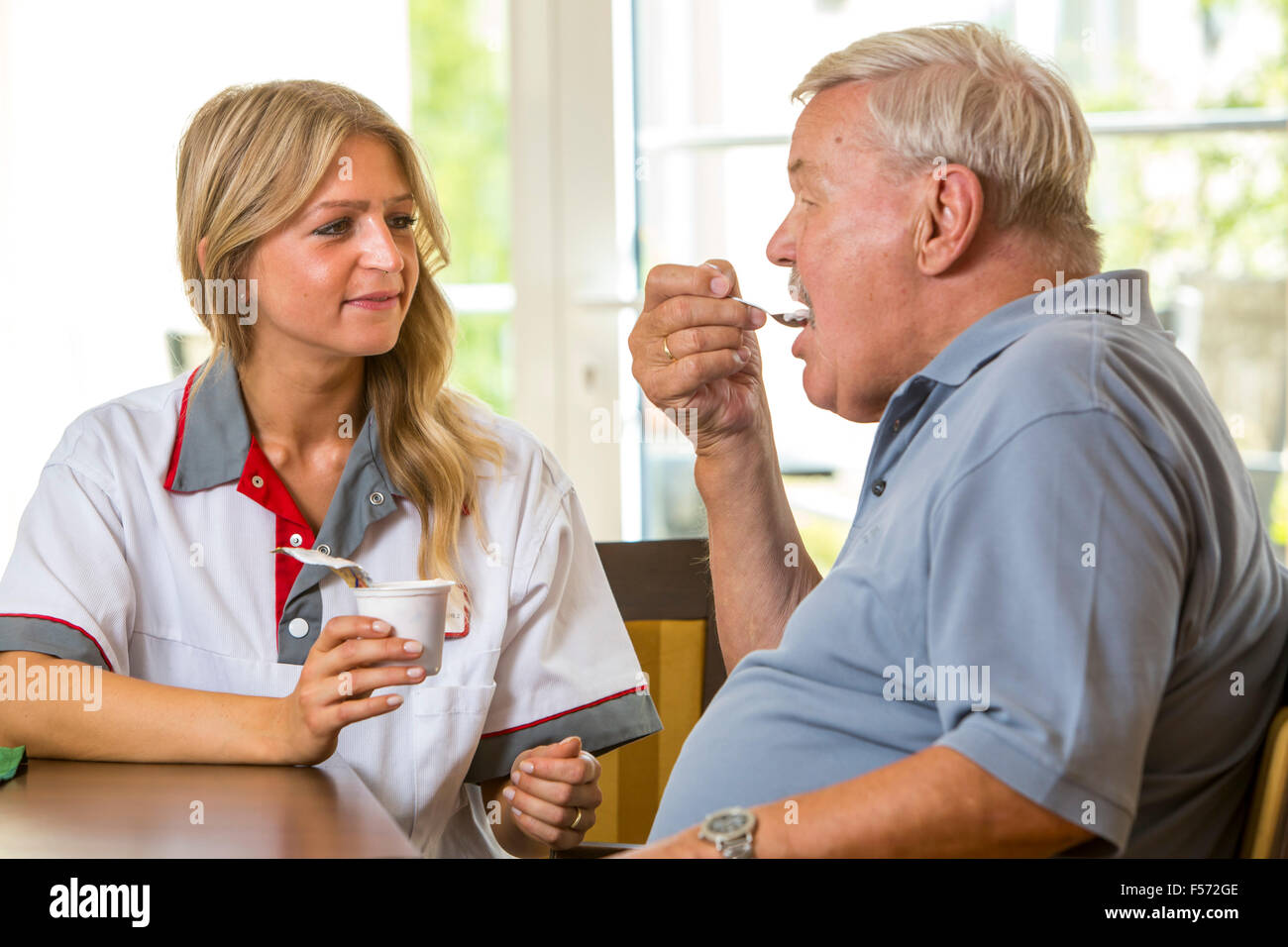 Elderly care in a nursing home, nurse helps an elderly man eating his ...