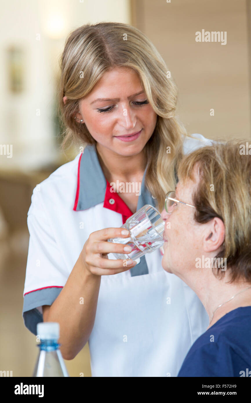 Elderly care in a nursing home, nurse helps an elderly woman drinking a ...