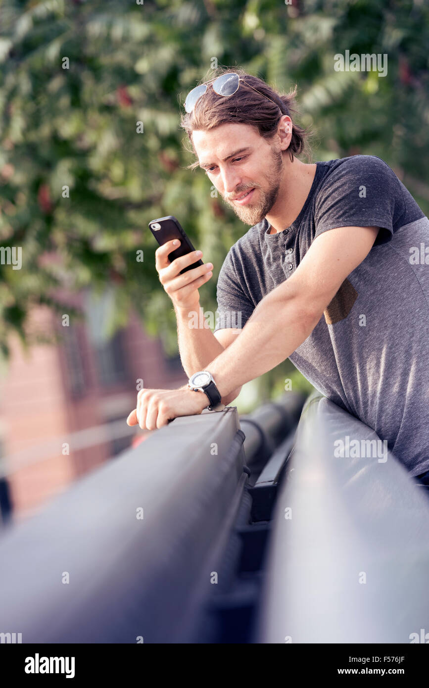 A young man leaning on a park railing checking his cell phone Stock ...